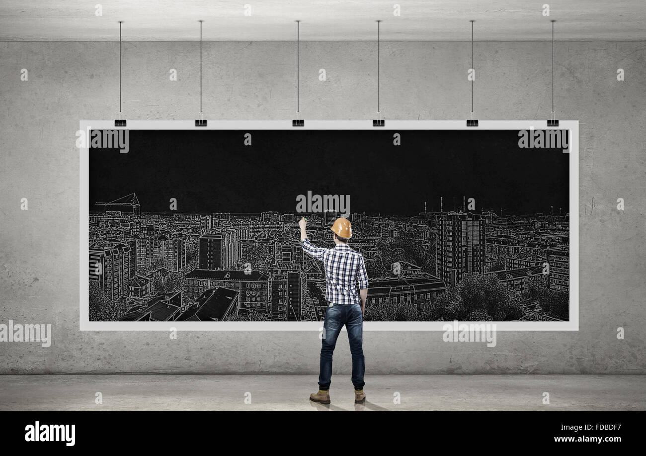 Rear view of man engineer in helmet drawing on chalkboard Stock Photo ...