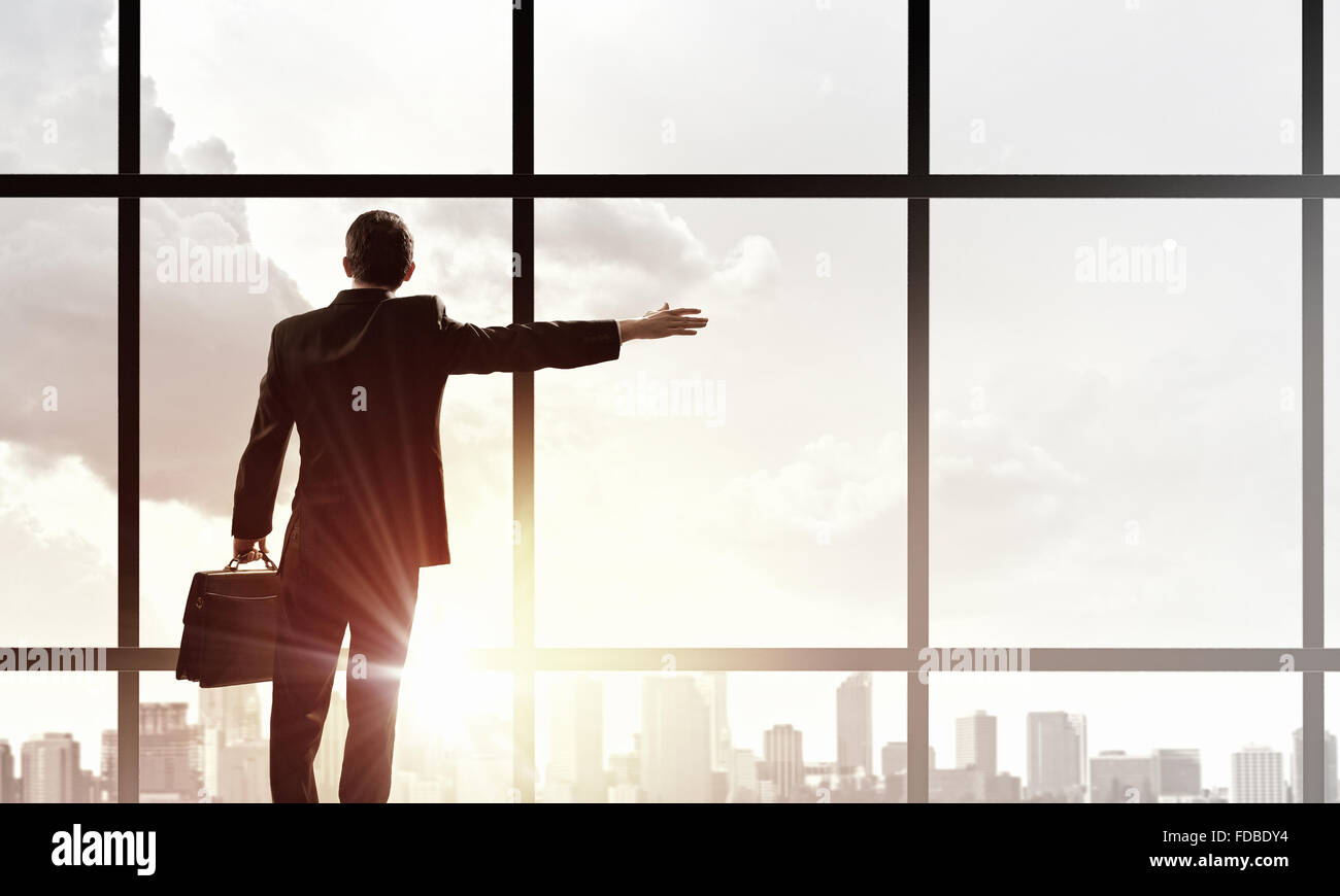 Back view of businessman looking on sunrise in office window and ...
