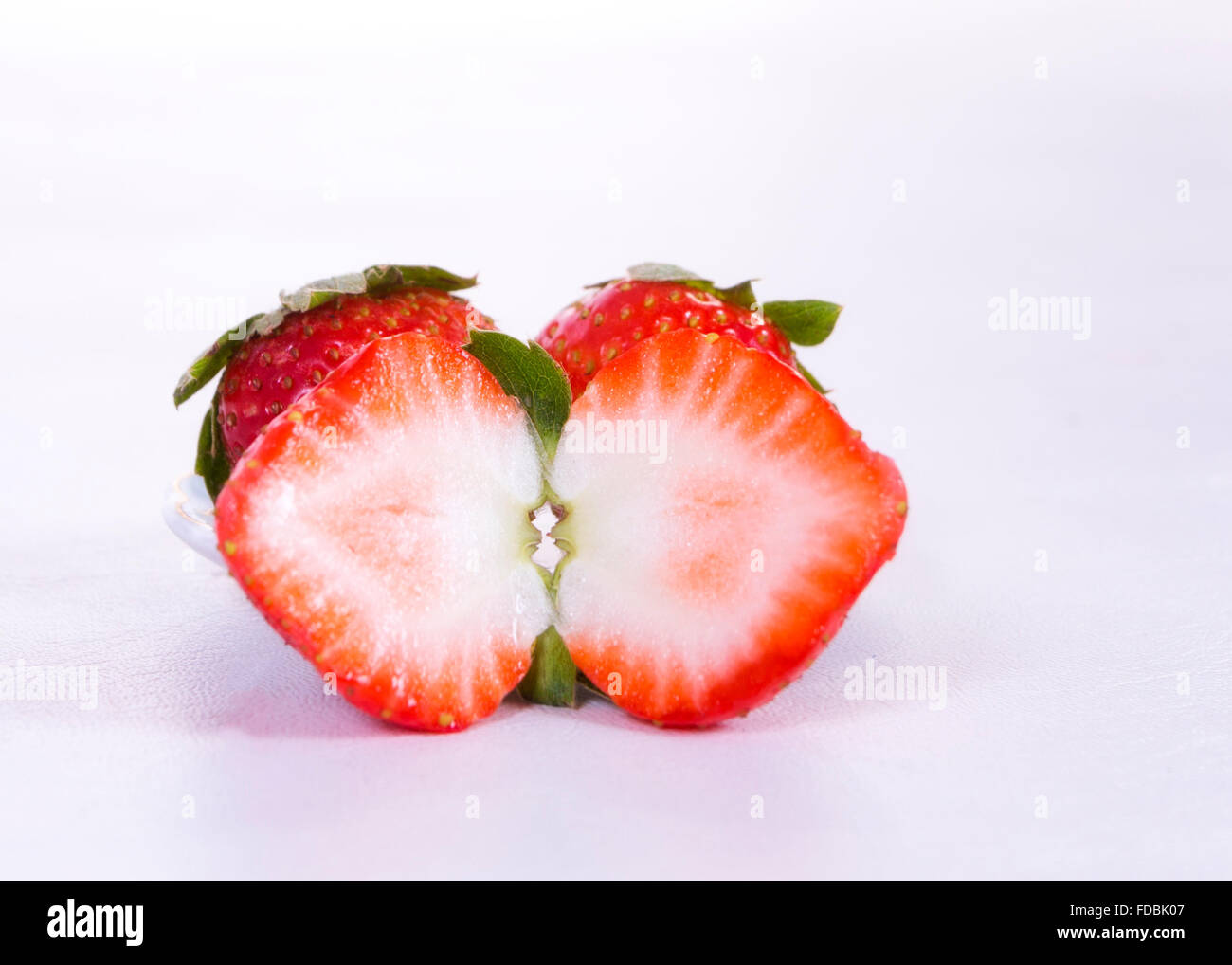 a strawberry chopped in half and two strawberries behind this more, all ...