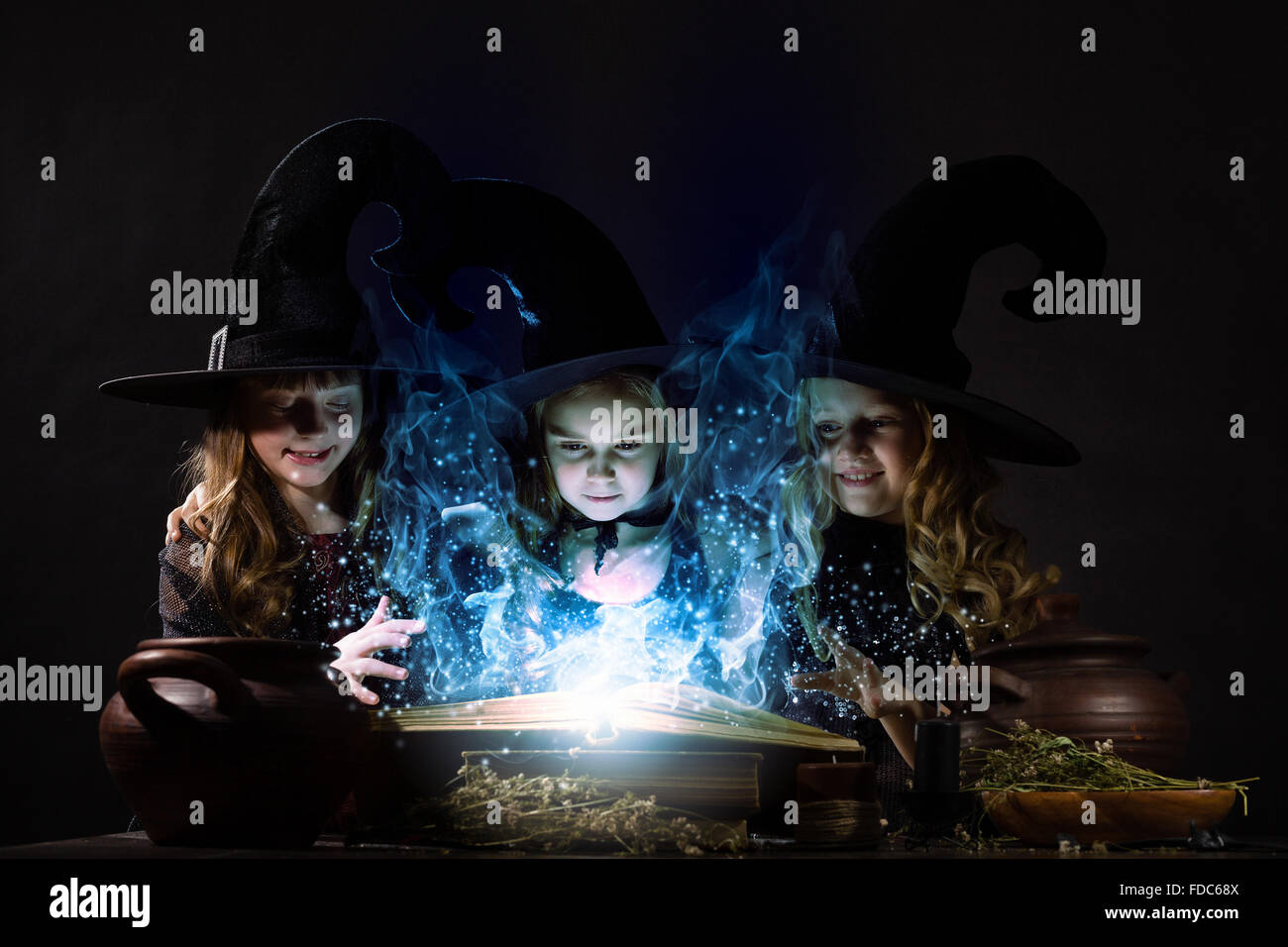 Three little Halloween witches reading spell above pot Stock Photo - Alamy