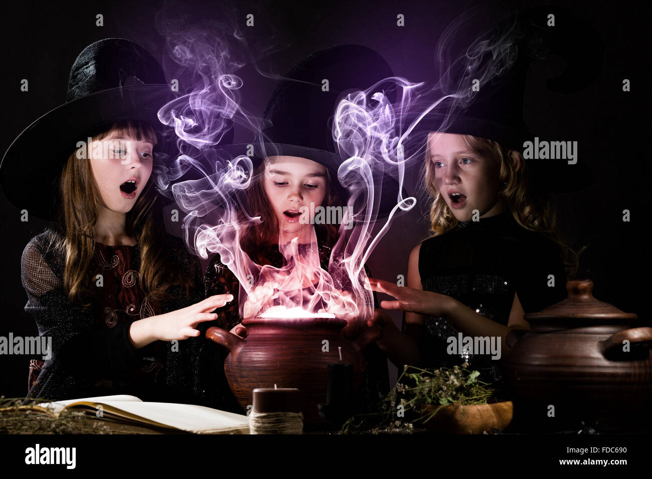 Three little Halloween witches reading spell above pot Stock Photo - Alamy