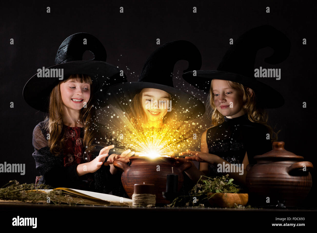 Three little Halloween witches reading spell above pot Stock Photo - Alamy