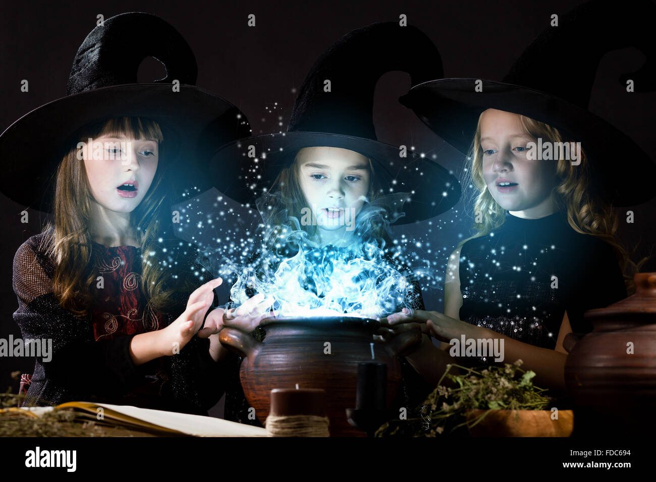 Three little Halloween witches reading spell above pot Stock Photo - Alamy