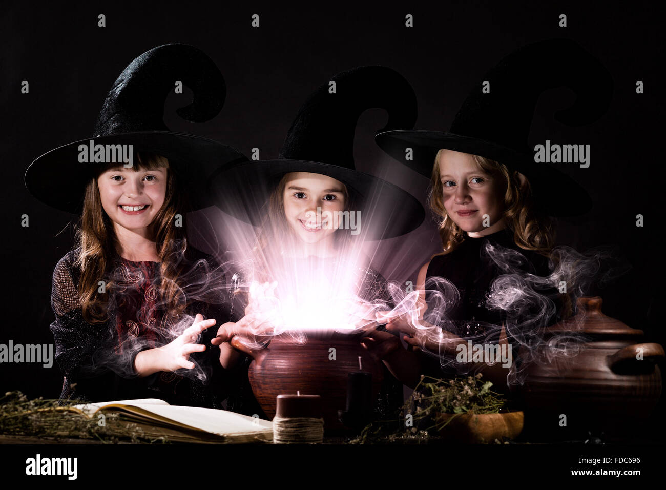 Three little Halloween witches reading spell above pot Stock Photo - Alamy