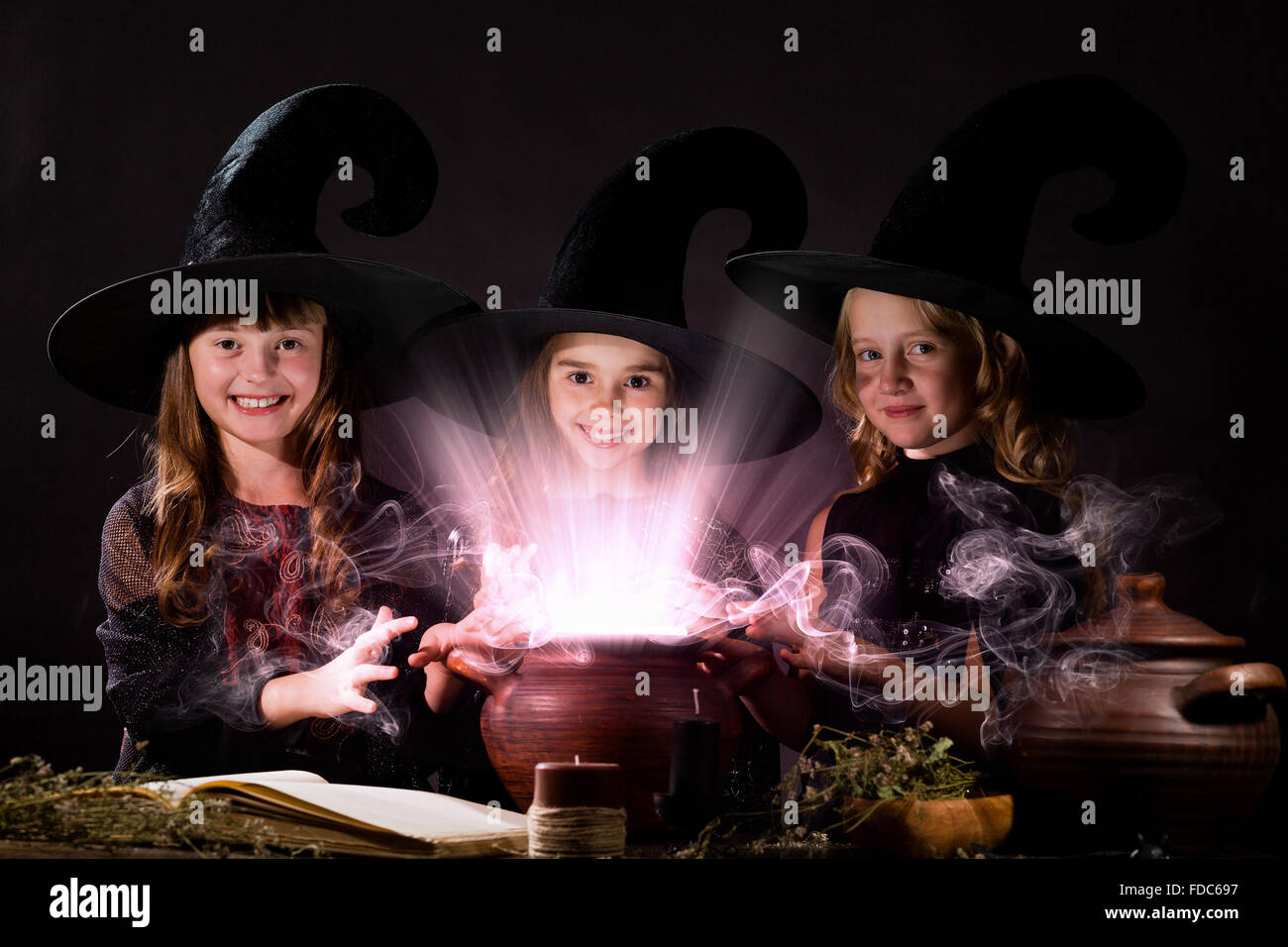 Three little Halloween witches reading spell above pot Stock Photo - Alamy