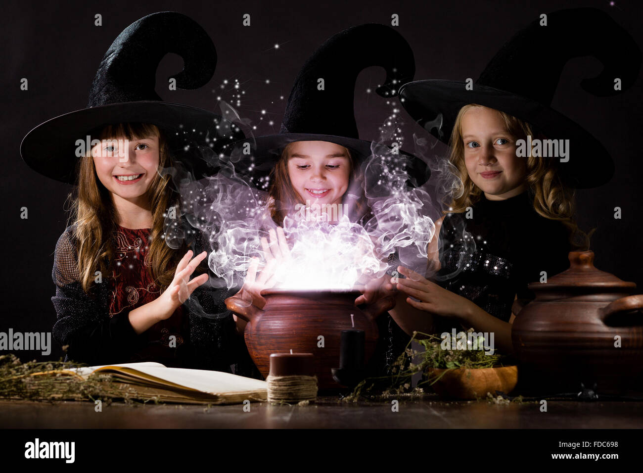 Three little Halloween witches reading spell above pot Stock Photo - Alamy