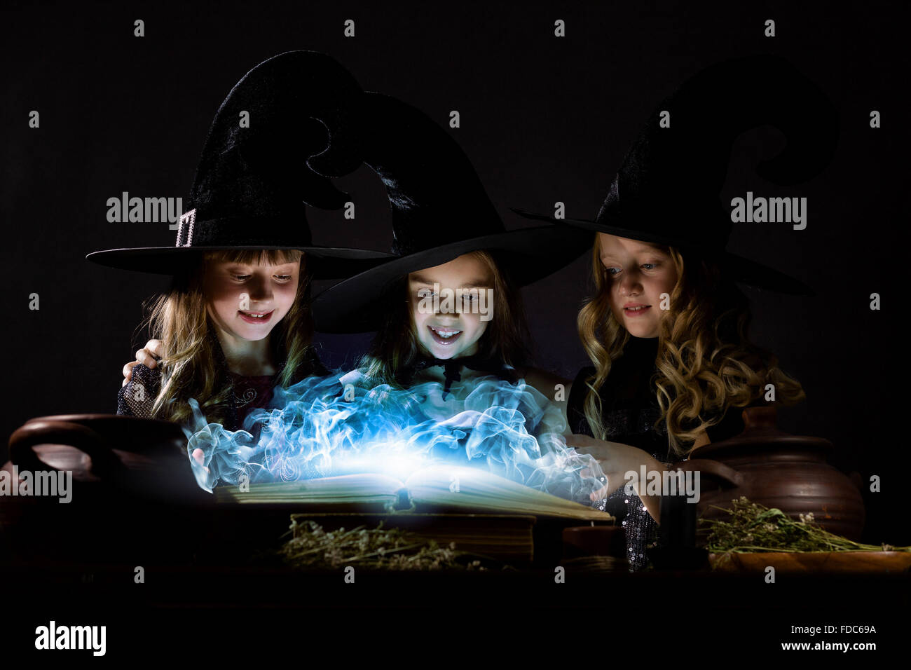 Three little Halloween witches reading spell above pot Stock Photo - Alamy