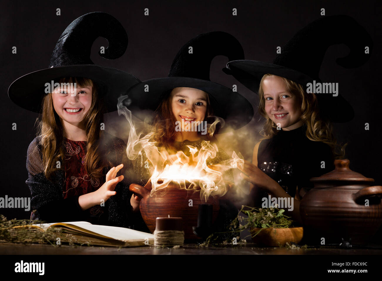 Three little Halloween witches reading spell above pot Stock Photo - Alamy
