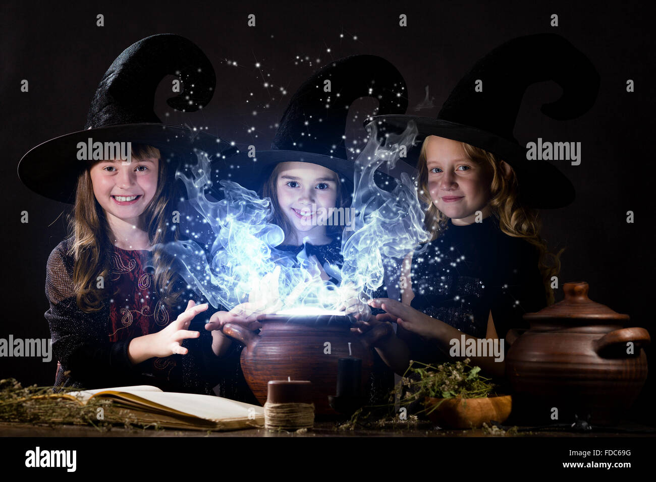 Three little Halloween witches reading spell above pot Stock Photo - Alamy