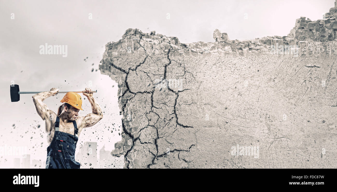 Strong man in uniform breaking brick wall with hammer Stock Photo - Alamy
