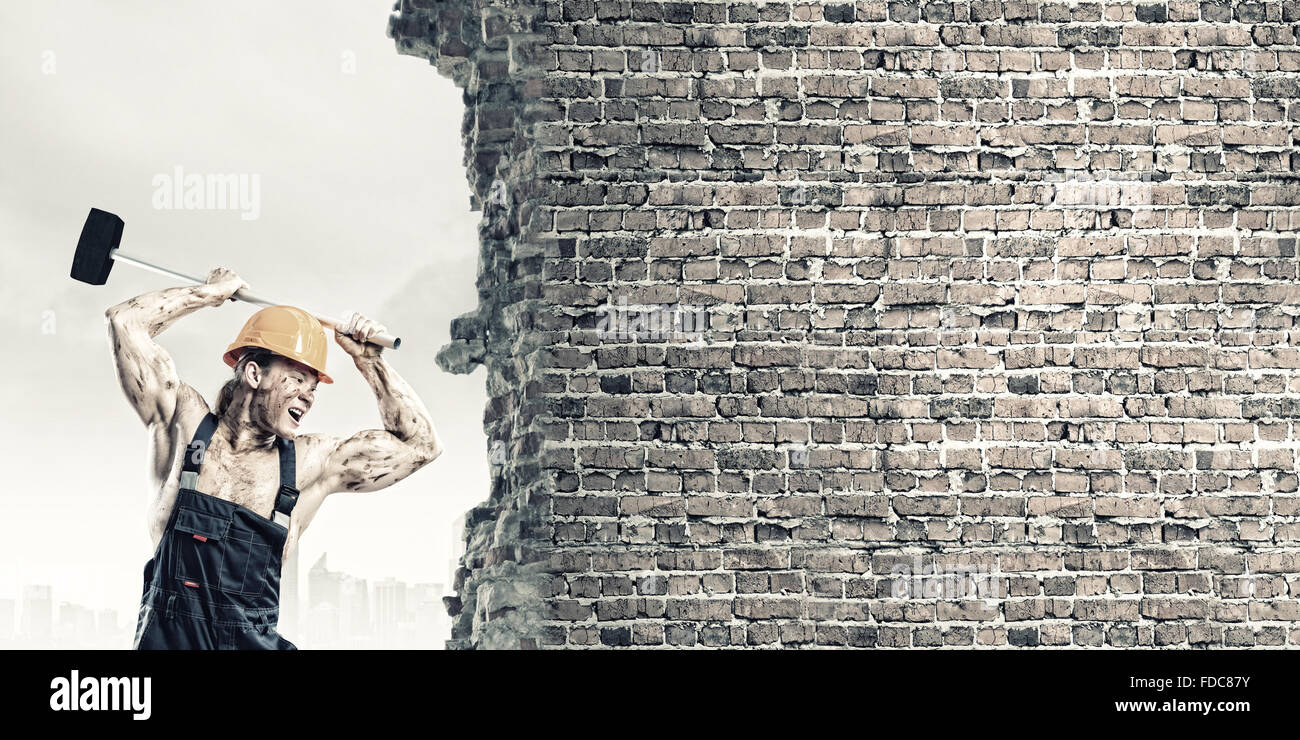 Strong man in uniform breaking brick wall with hammer Stock Photo - Alamy