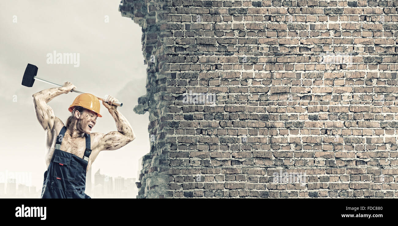 Strong man in uniform breaking brick wall with hammer Stock Photo - Alamy