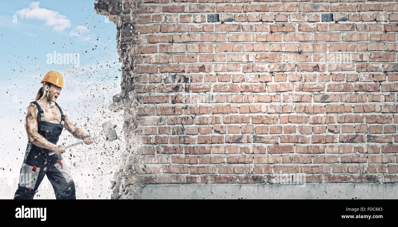 Strong man in uniform breaking brick wall with hammer Stock Photo - Alamy