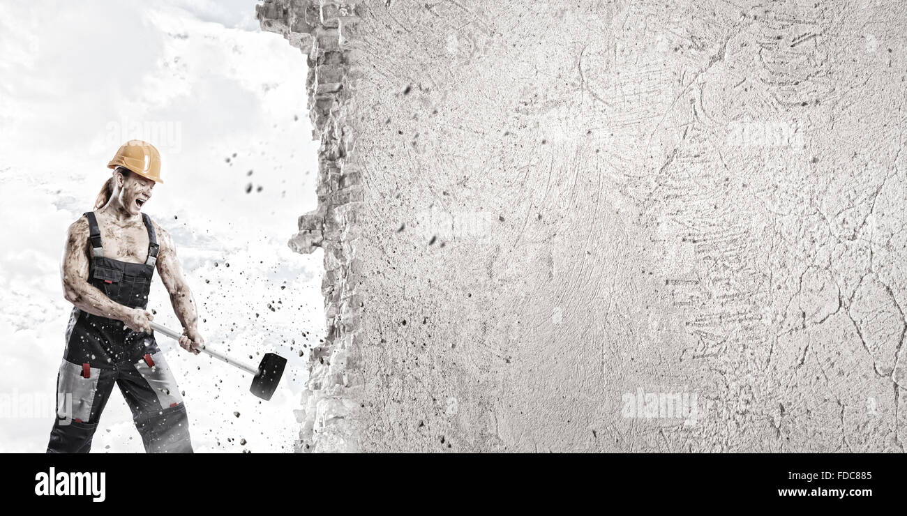 Strong man in uniform breaking brick wall with hammer Stock Photo - Alamy