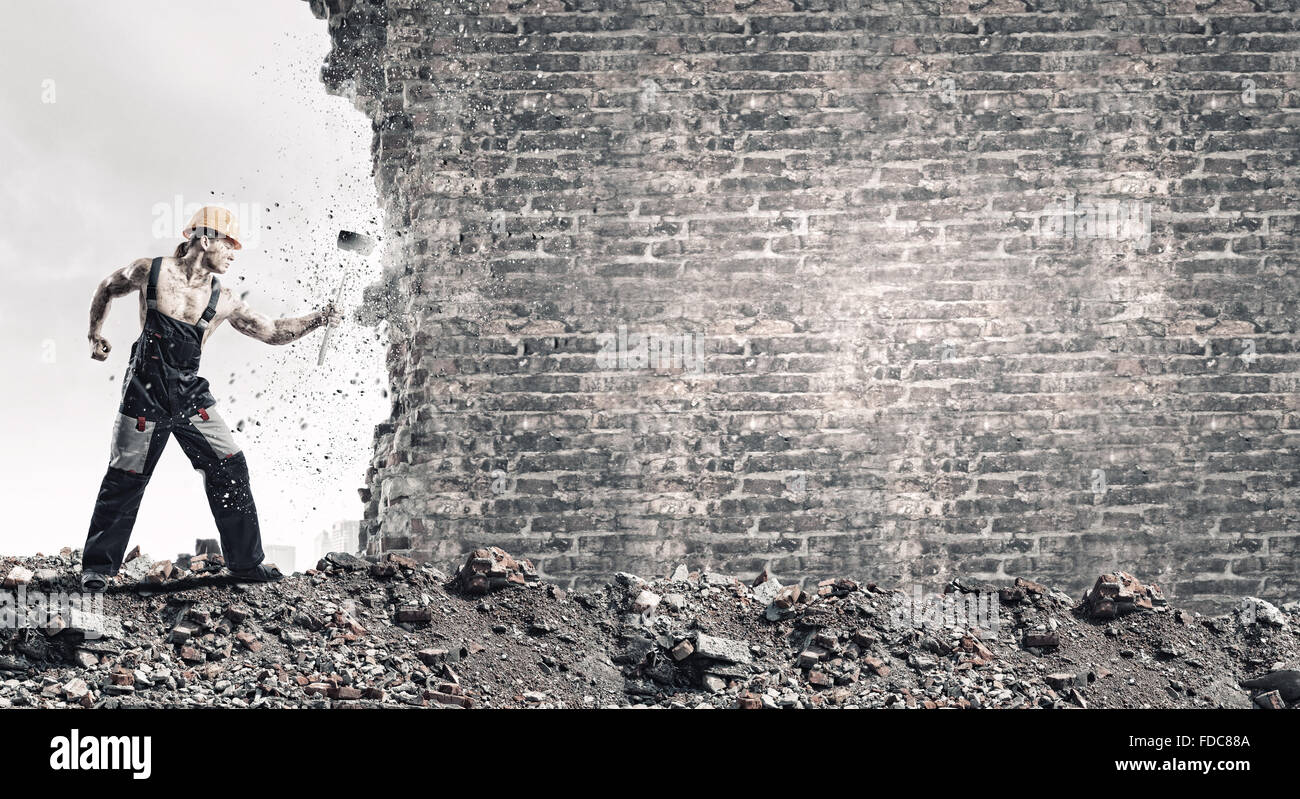 Strong man in uniform breaking brick wall with hammer Stock Photo - Alamy