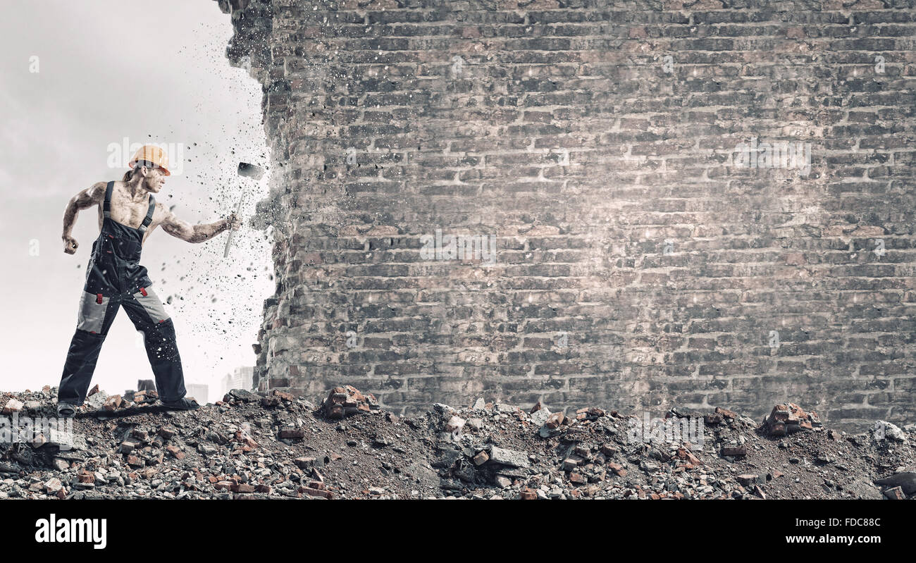 Strong man in uniform breaking brick wall with hammer Stock Photo - Alamy