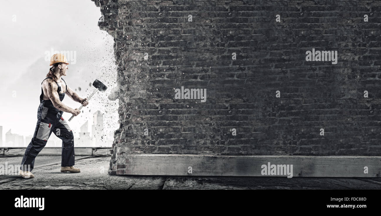 Strong man in uniform breaking brick wall with hammer Stock Photo - Alamy