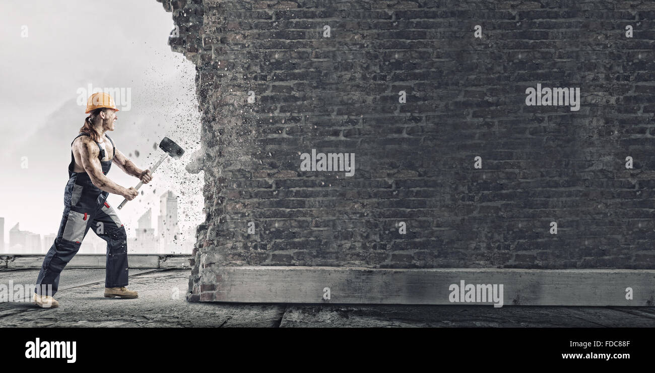 Strong man in uniform breaking brick wall with hammer Stock Photo - Alamy