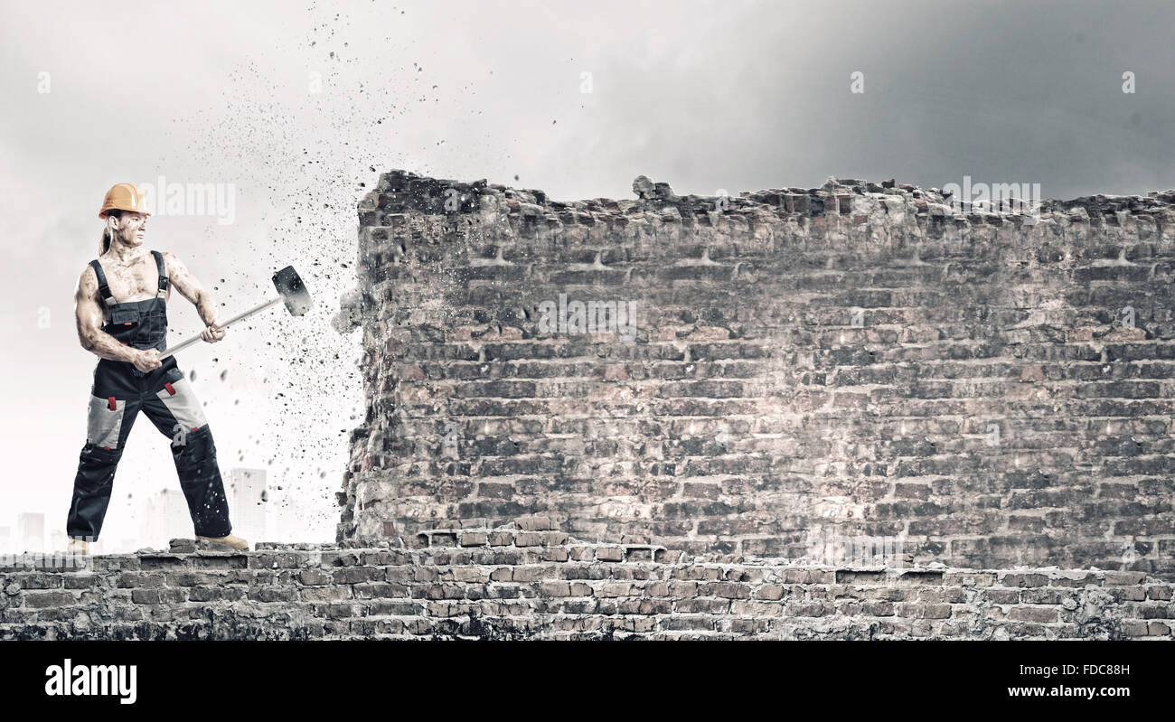 Strong man in uniform breaking brick wall with hammer Stock Photo - Alamy