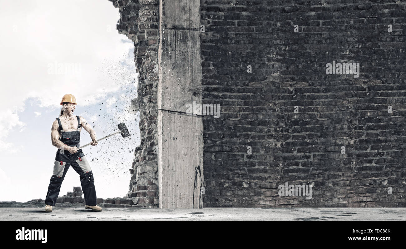 Strong man in uniform breaking brick wall with hammer Stock Photo - Alamy