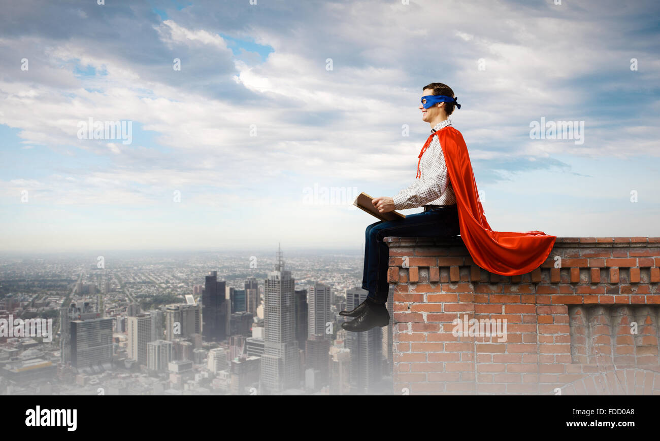 Young man in superhero costume reading book Stock Photo - Alamy