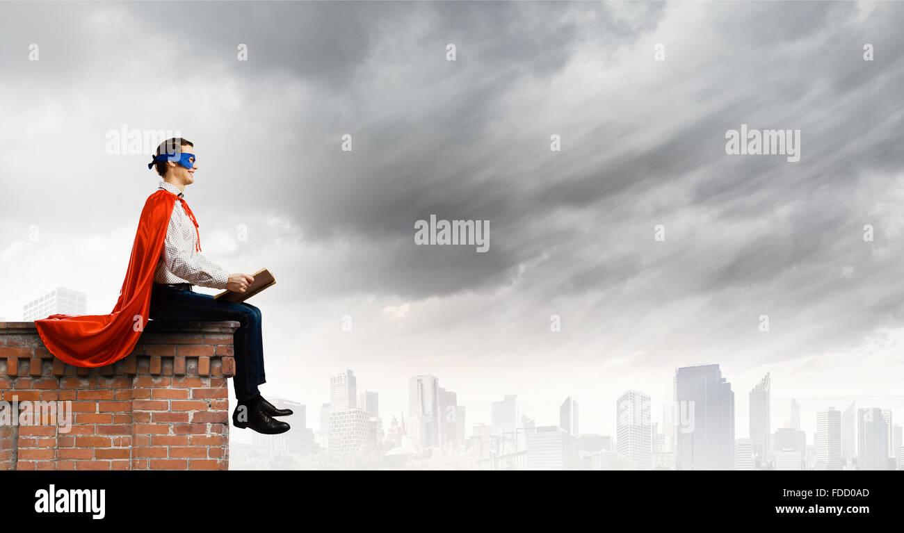 Young man in superhero costume reading book Stock Photo - Alamy