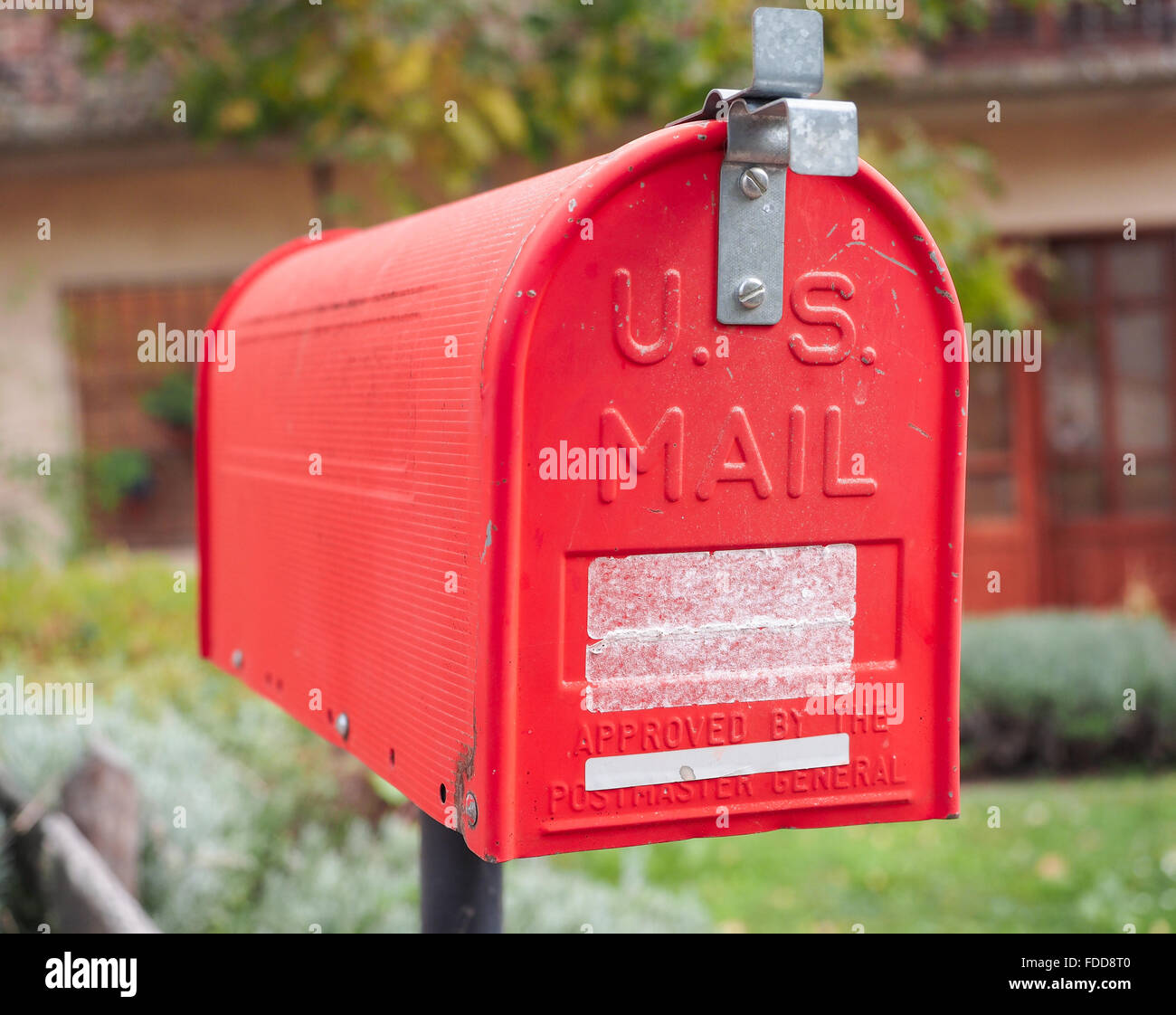 An old home letter box, red painted, with background of rural house ...