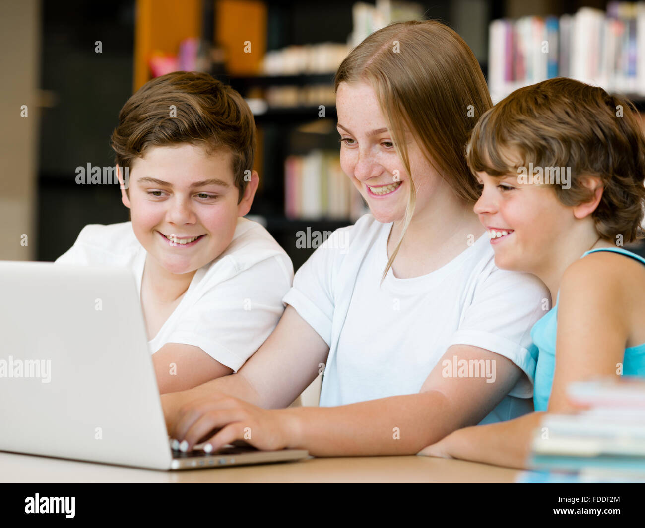 Three kids in library with notebook Stock Photo - Alamy