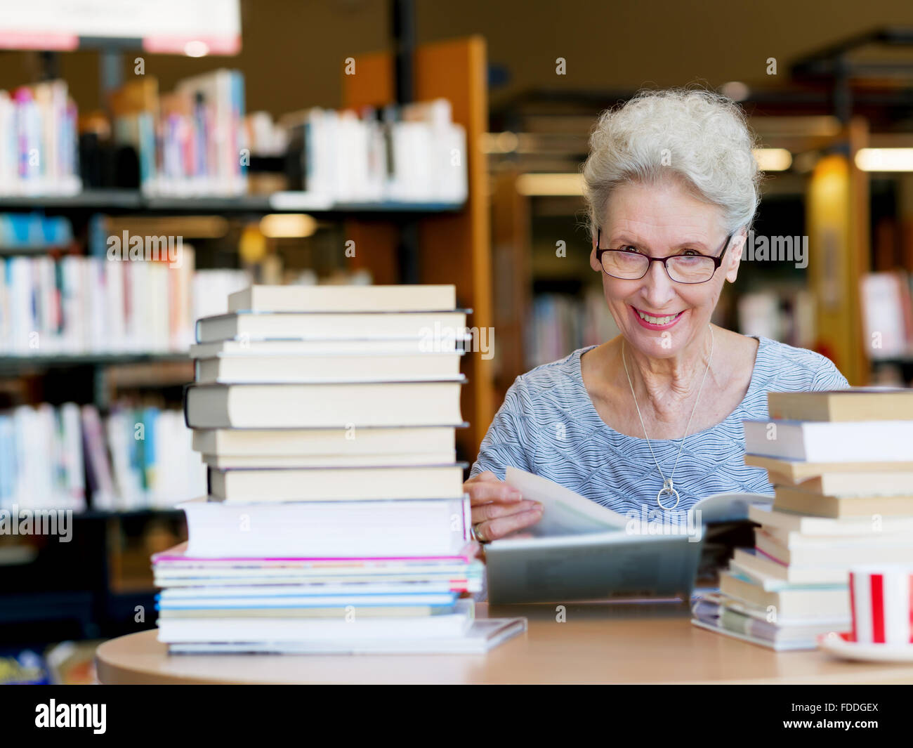 Elderly lady reading books in library Stock Photo - Alamy