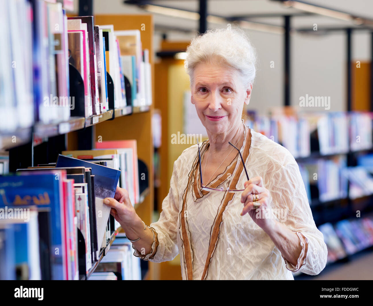 Elderly lady standing next to book shelves in library Stock Photo - Alamy