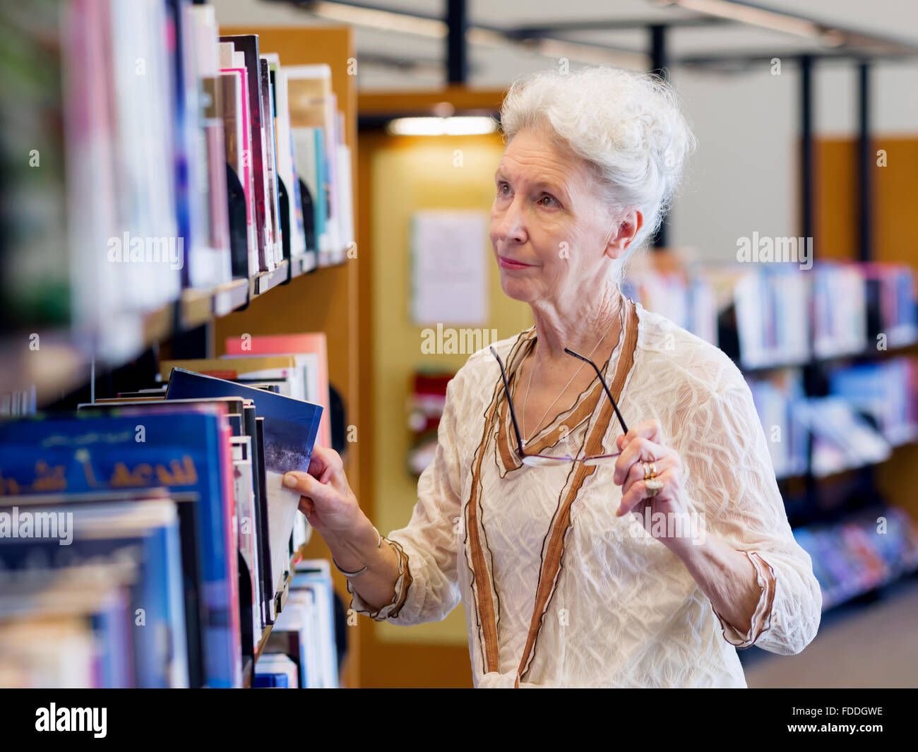 Elderly lady standing next to book shelves in library Stock Photo - Alamy