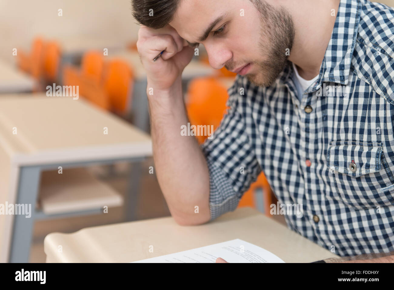 Portrait Of Young Male College Student With Book Sitting In Classroom ...