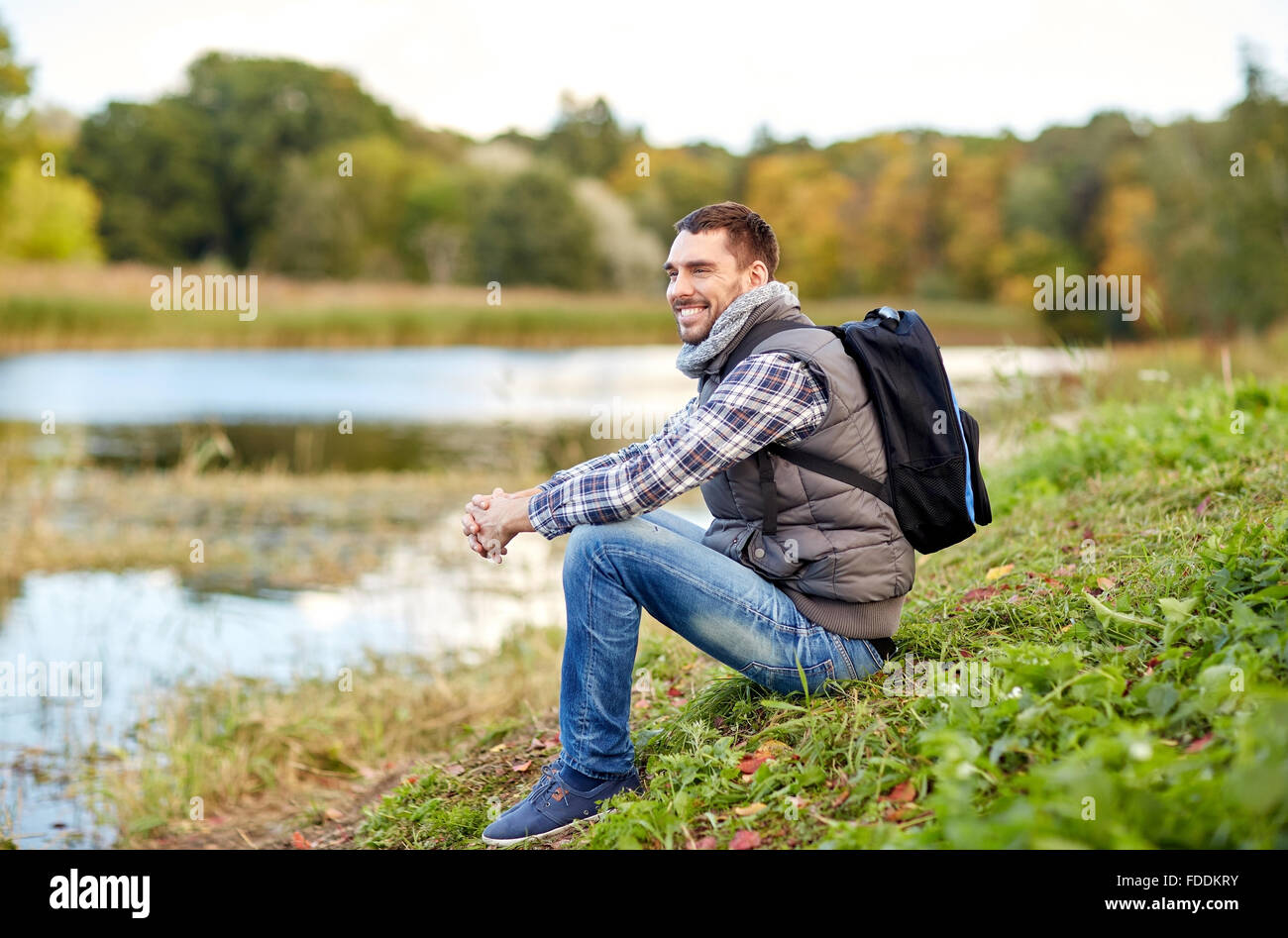 smiling man with backpack resting on river bank Stock Photo - Alamy
