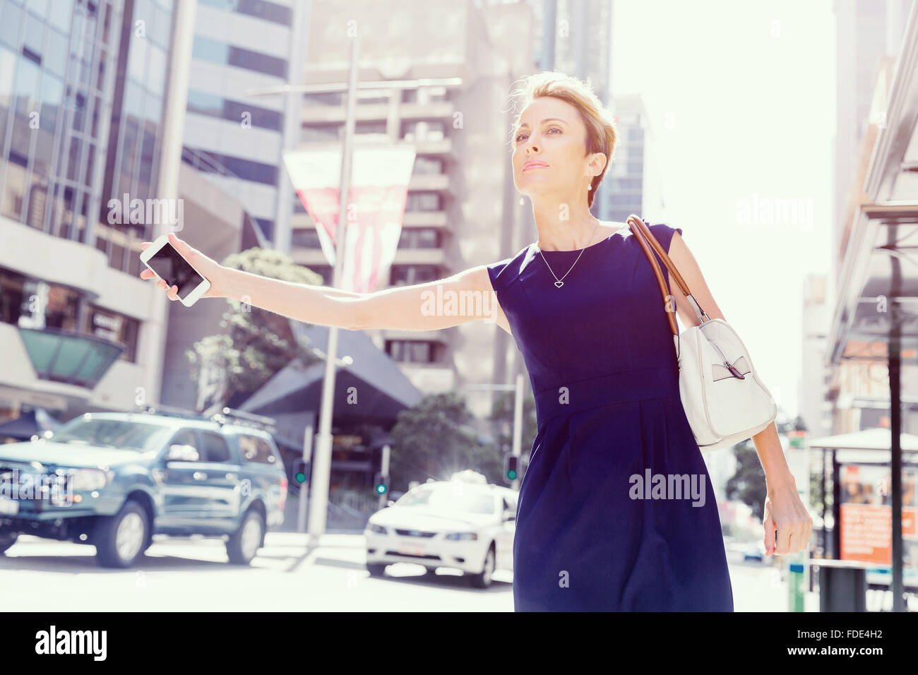 Businesswoman in a city street waving for taxi Stock Photo - Alamy