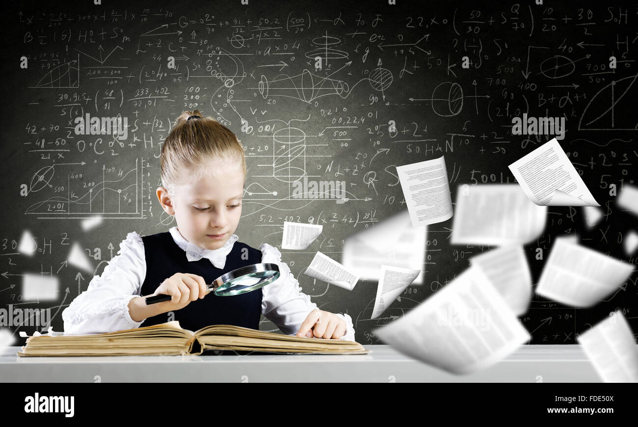 Schoolgirl examining opened book with magnifying glass Stock Photo - Alamy