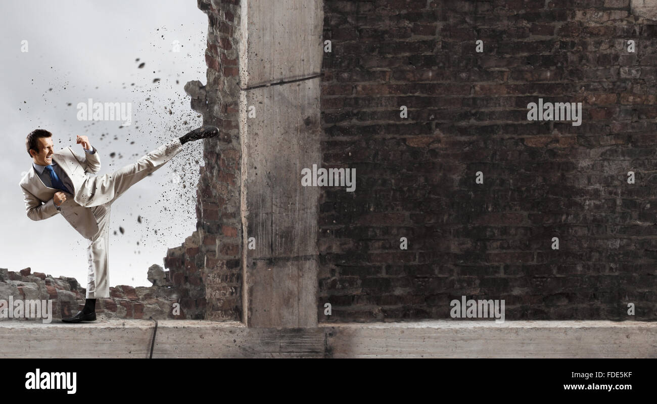 Businessman breaking stone wall with karate kick Stock Photo - Alamy