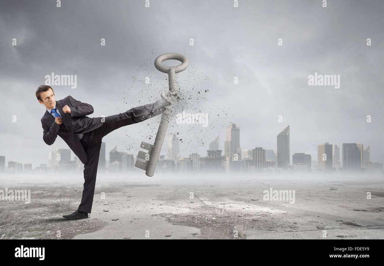 Angry businessman crashing stone key with kick Stock Photo - Alamy