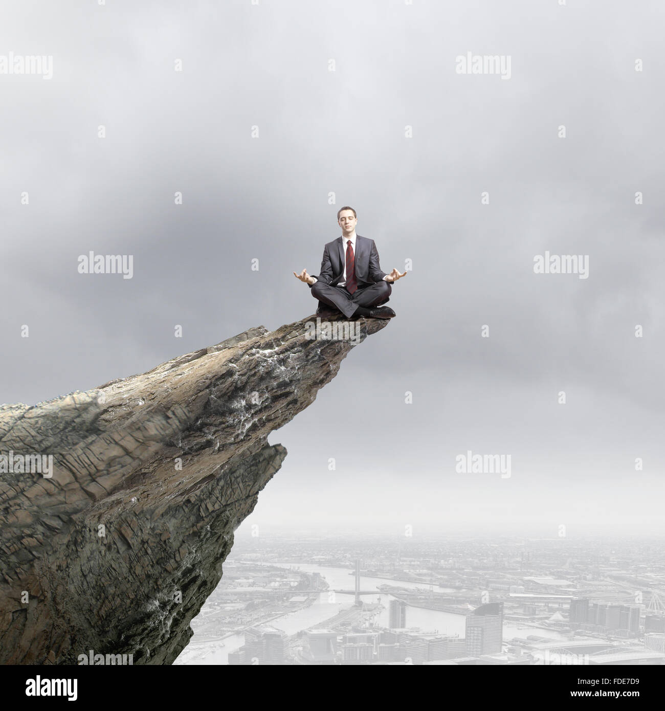 Young businessman sitting lotus pose on edge of rock mountain Stock ...