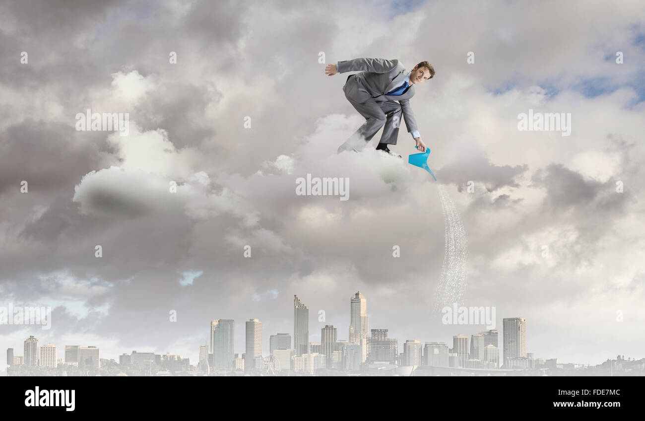 Young businessman standing on cloud and watering something below Stock ...