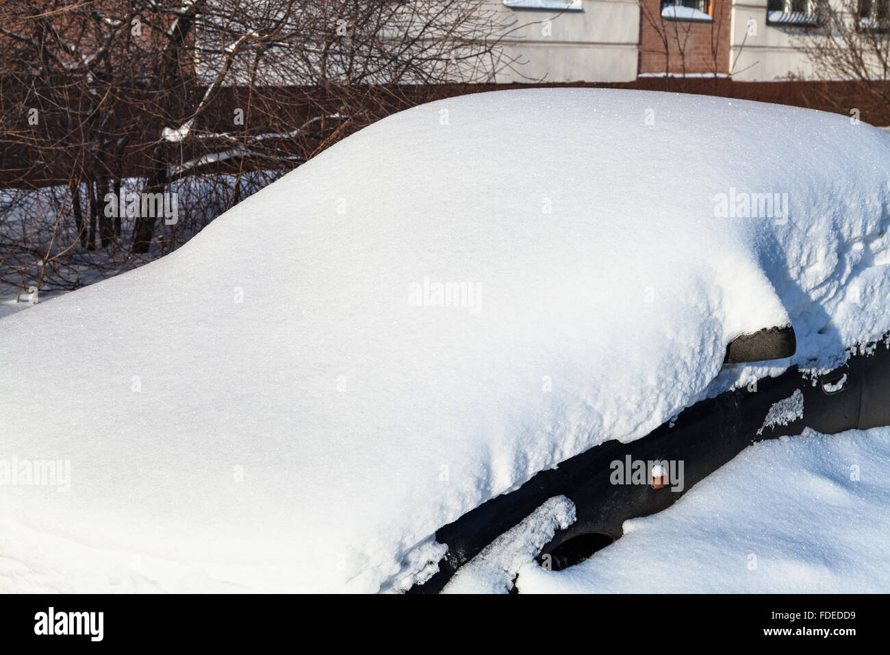 black car under snowdrift close up in parking lot near urban house ...