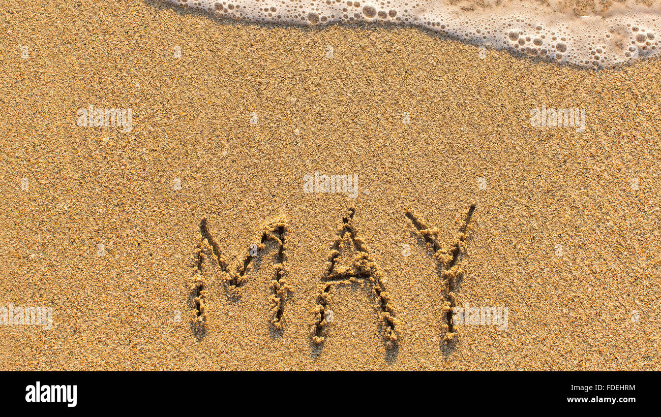 Inscription MAY on a gentle beach sand with the soft wave (months of ...