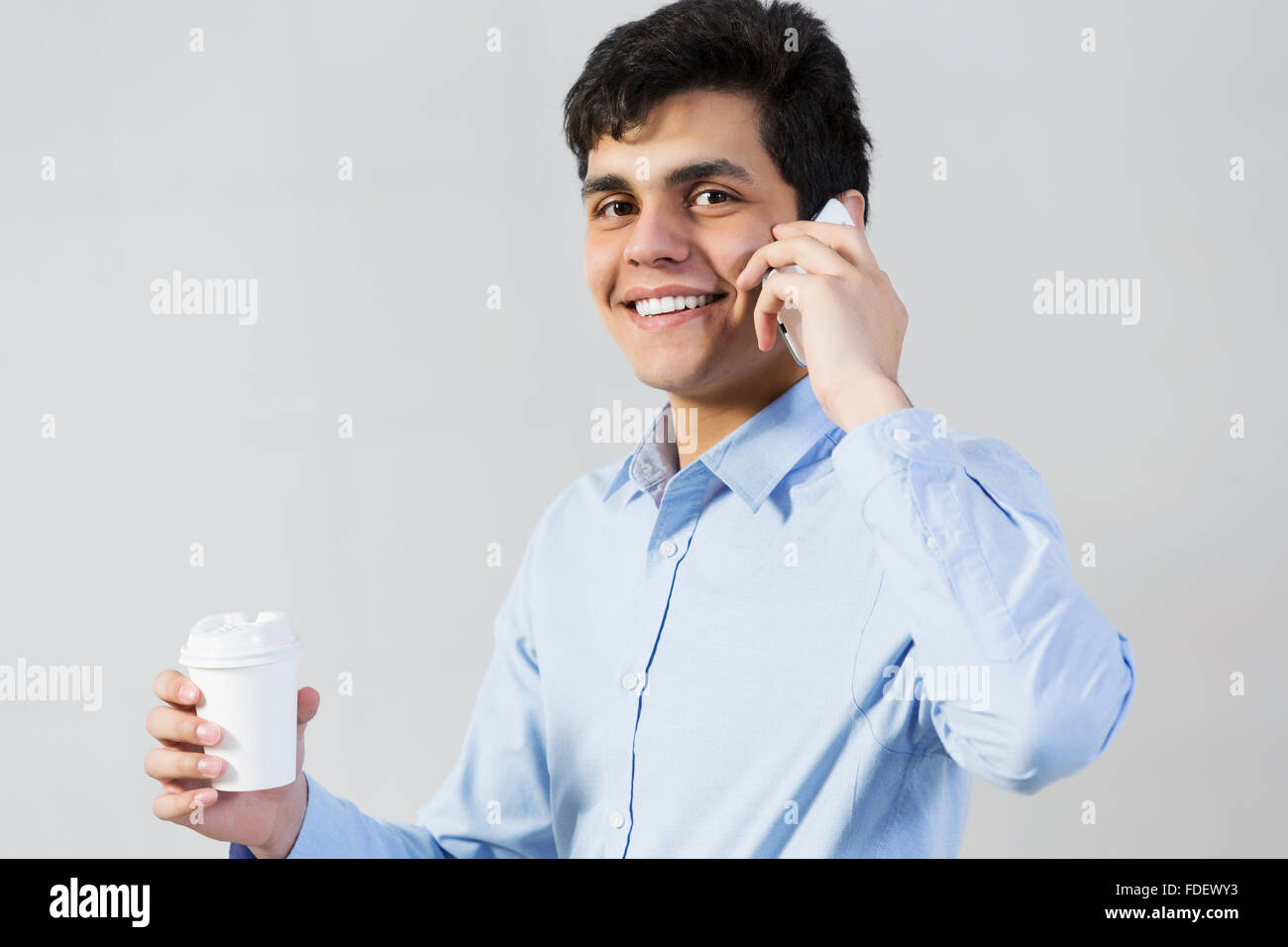 Young man with coffee in hand talking on mobile phone Stock Photo - Alamy