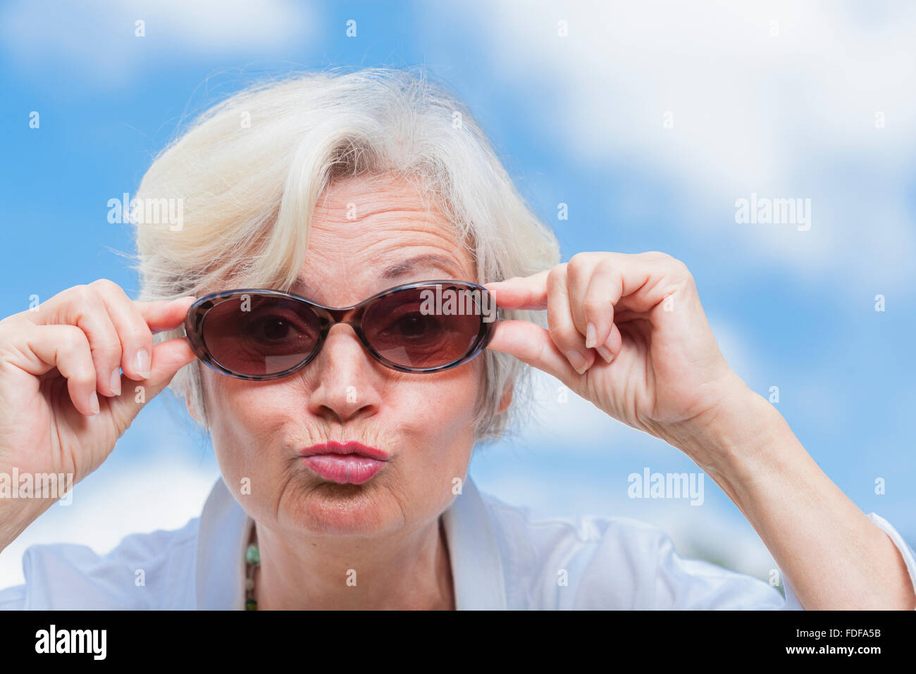 senior old woman smiling with sunglasses in front of blue summer sky ...