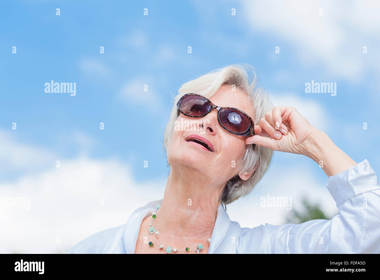 senior old woman smiling with sunglasses in front of blue summer sky ...