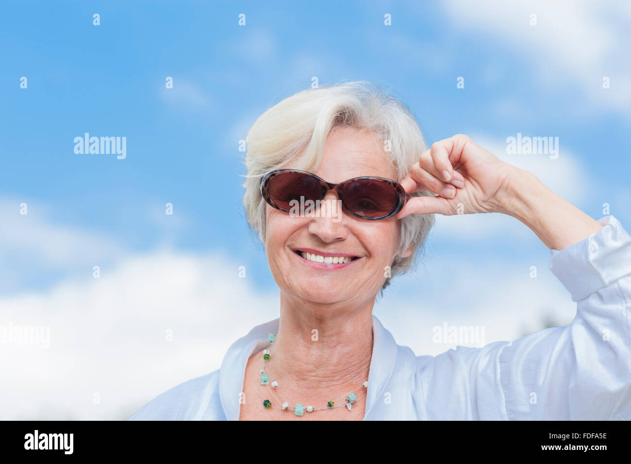 senior old woman smiling with sunglasses in front of blue summer sky ...
