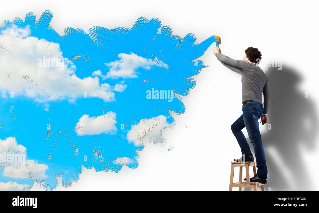 Young man drawing a cloudy blue sky on the wall Stock Photo - Alamy