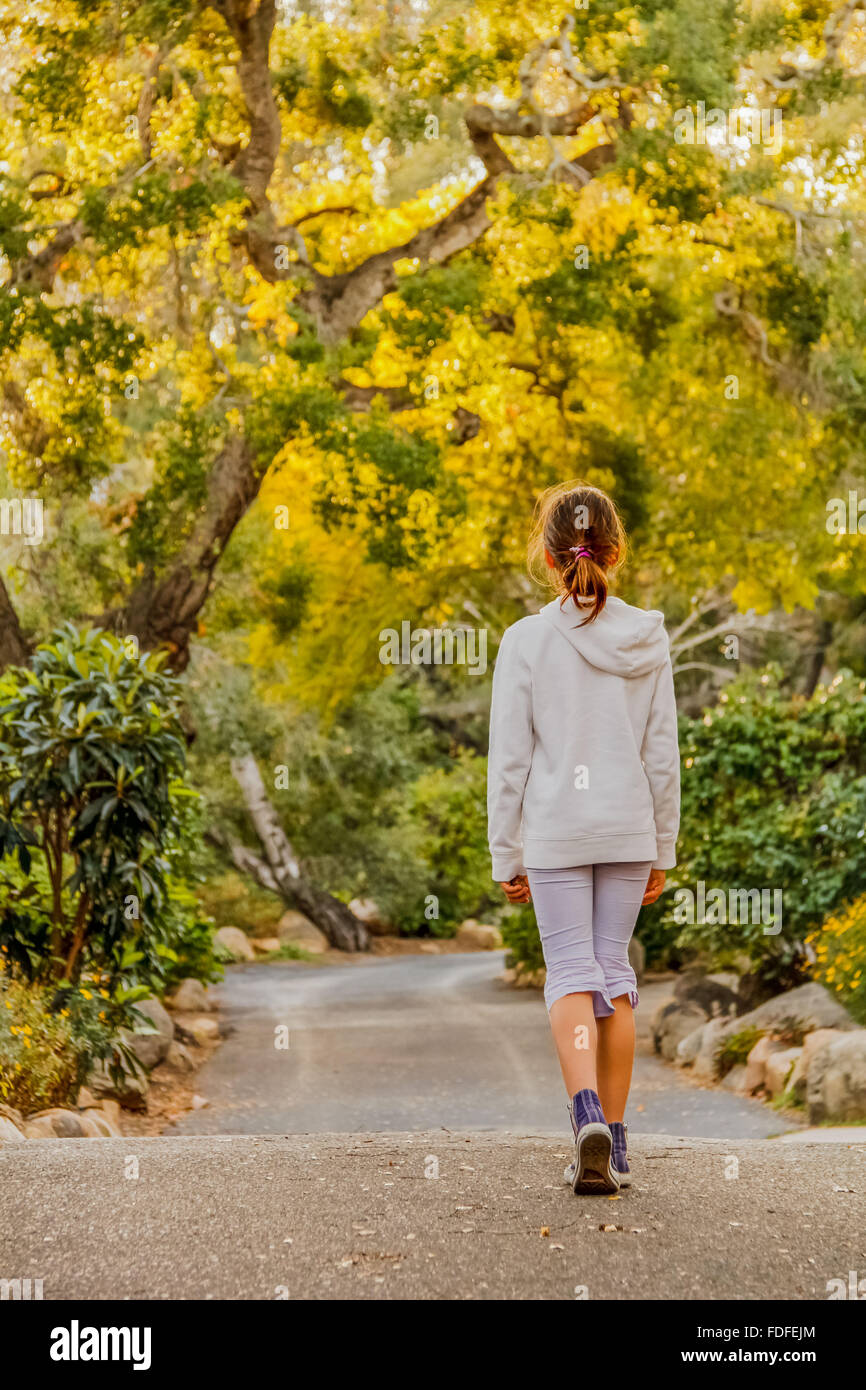 girl entering a path surrounded by trees where light turns the leaves ...