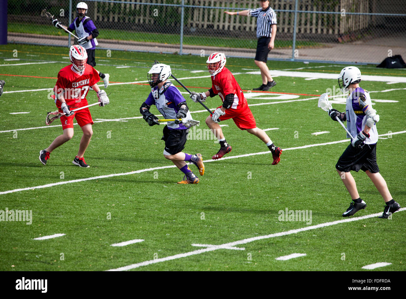 Teen lacrosse boys match running down field with ball wearing helmets ...