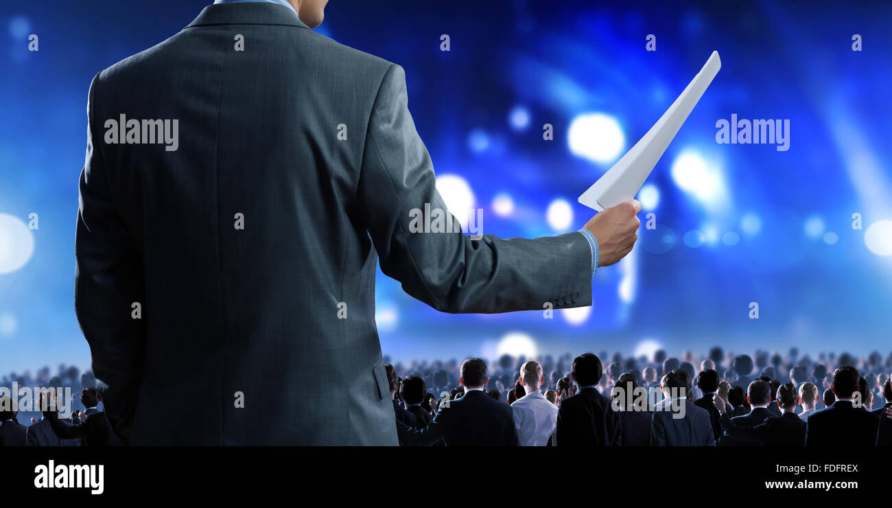Back view of businessman speaker standing on podium with papers in hand ...