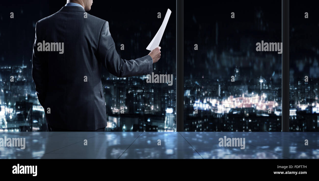 Businessman standing against office window reading documents Stock ...
